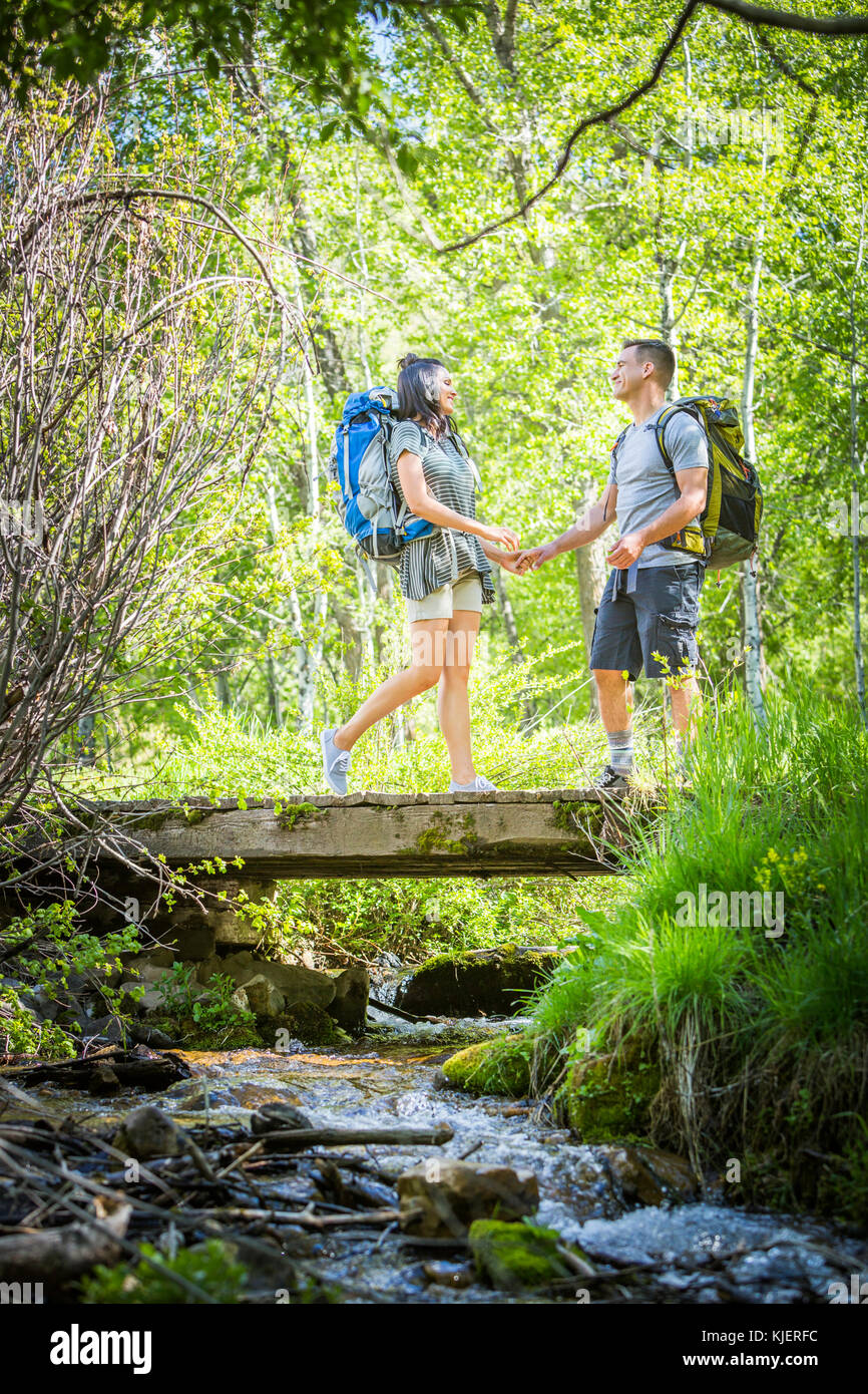 Couple carrying backpacks across bridge in woods Stock Photo - Alamy