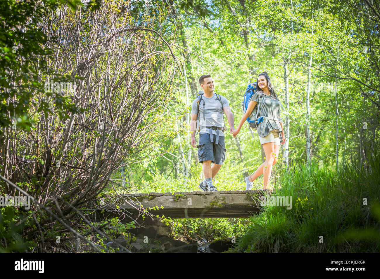 Couple carrying backpacks across bridge in woods Stock Photo - Alamy