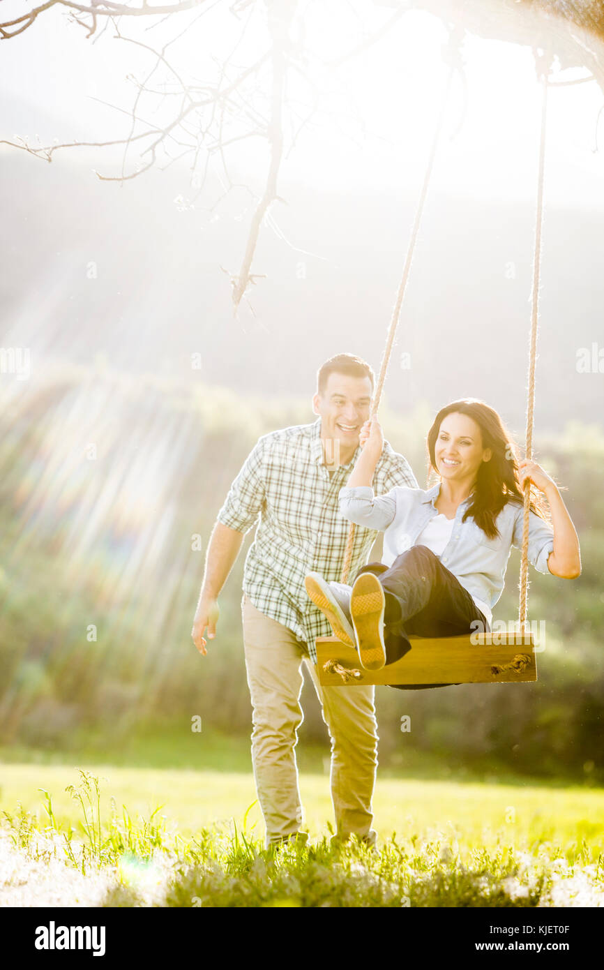 Man pushing woman swinging on tree swing Stock Photo - Alamy