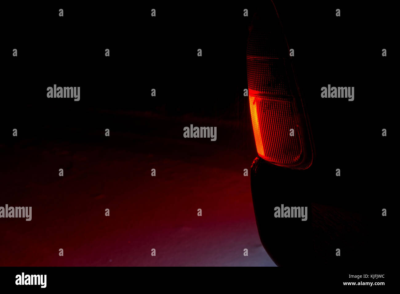 Winter abstract view from the back of a glowing red headlight of car ...