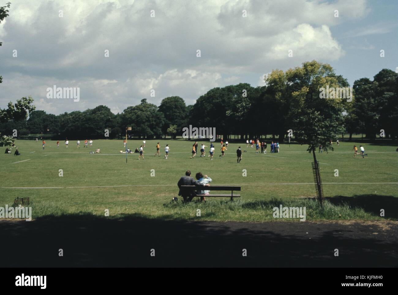 Two mature tourists siting on a bench and watching a large team of ...