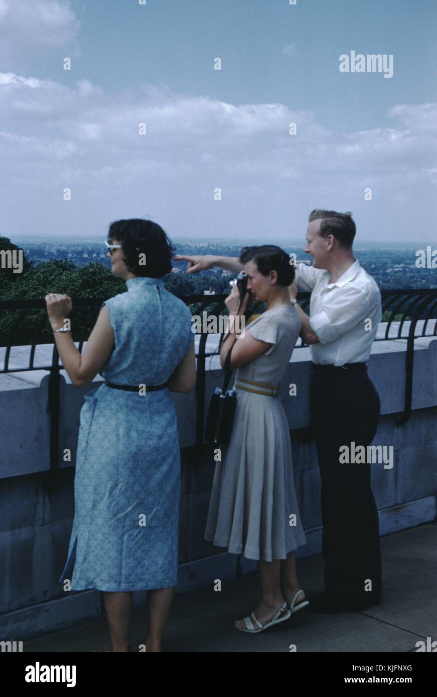 A photograph of three people looking over the ledge of a building, the ...