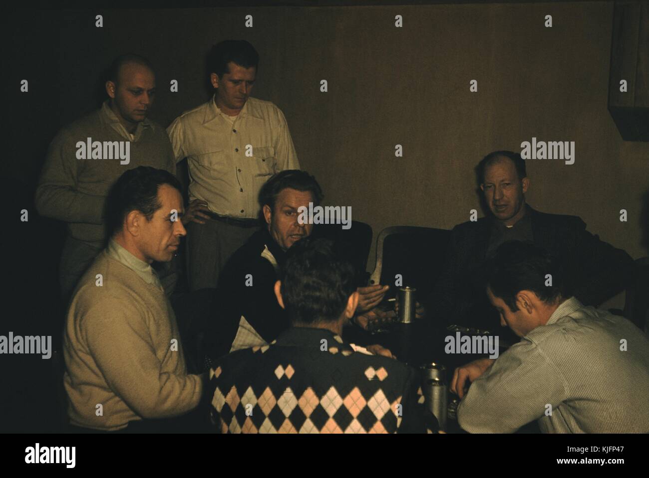 Group of seven men, five sitting around a card table drinking and ...