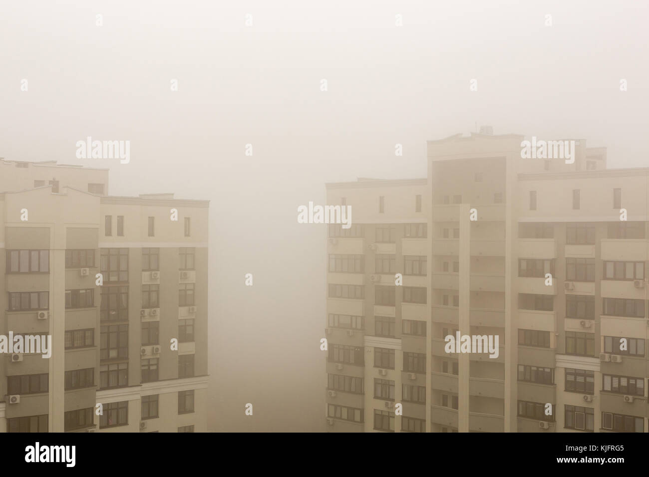 Top part of highrise modern apartment building facade during heavy fog ...