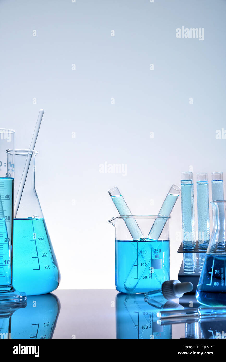 Laboratory glass chemical containers full of blue liquid on glass table ...