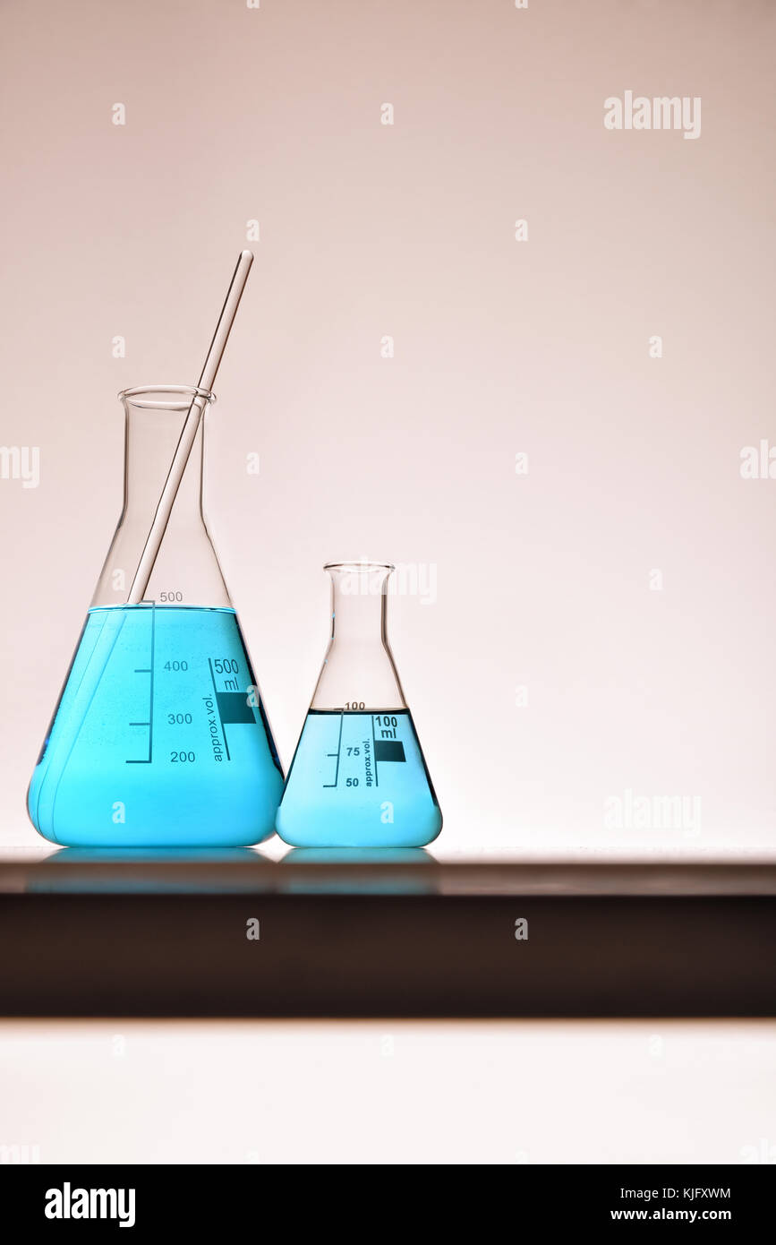 Laboratory glass chemical containers full of blue liquid on glass table ...