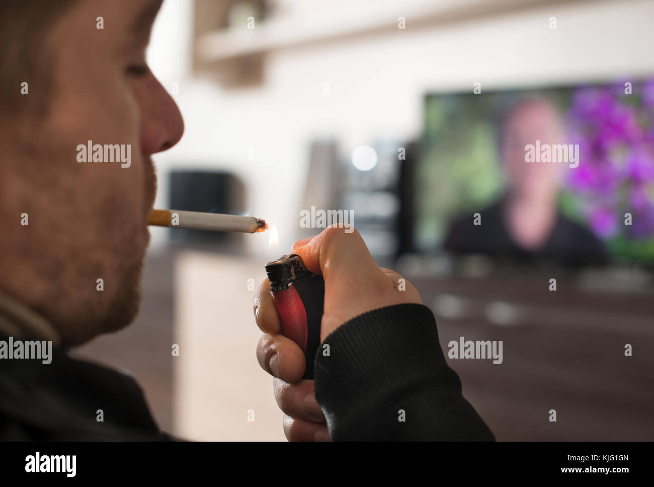 Young man lights a cigarette in front of TV Stock Photo - Alamy