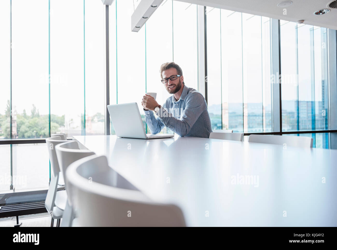 Man with laptop and cup of coffee sitting at conference table in office ...