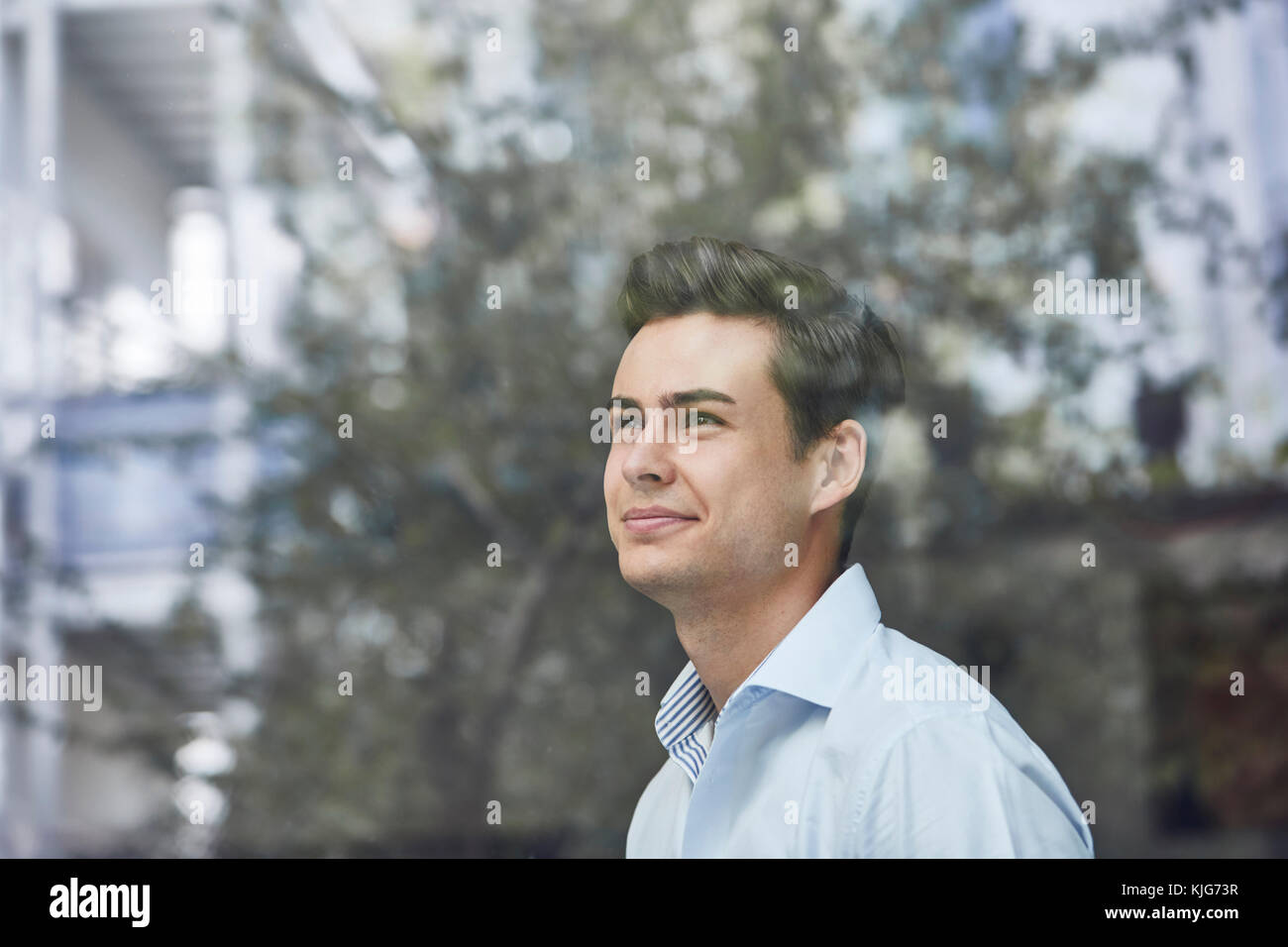 Portrait of smiling young businessman looking out of window Stock Photo ...