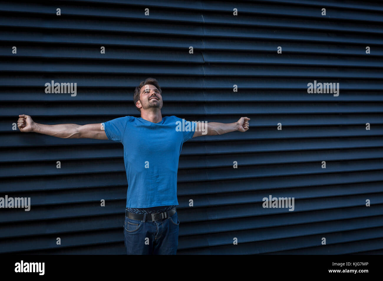 Man standing in front of roller shutter, looking up with arms ...