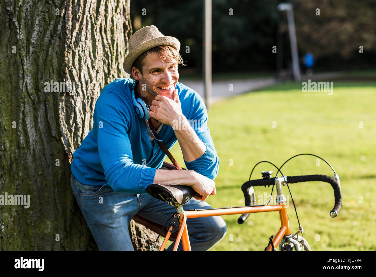 Portrait of laughing man with racing cycle leaning against tree trunk ...