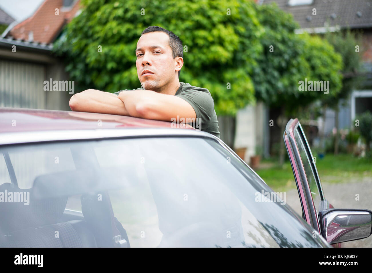 Portrait of serious man leaning on car roof Stock Photo - Alamy