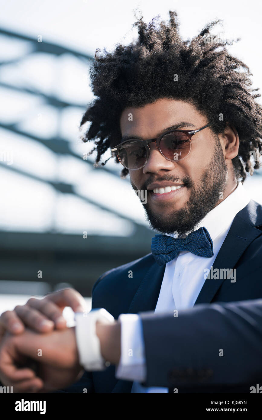 Smiling young man with sunglasses looking at his smartwatch Stock Photo ...