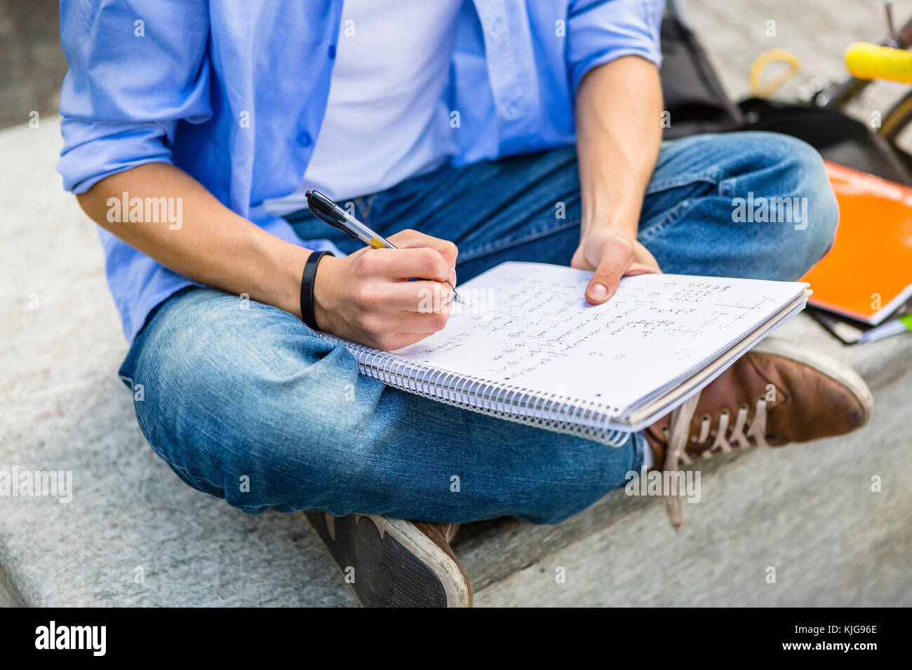 Young man sitting on bench writing on notepad, partial view Stock Photo ...