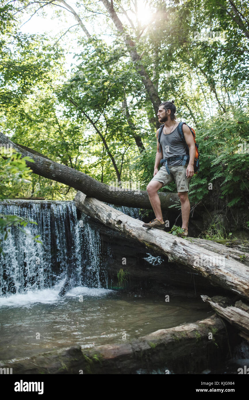 Young man standing on log at a waterfall in forest Stock Photo - Alamy