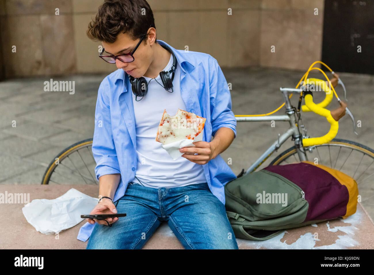 Young man eating pizza on a bench while looking at cell phone Stock ...