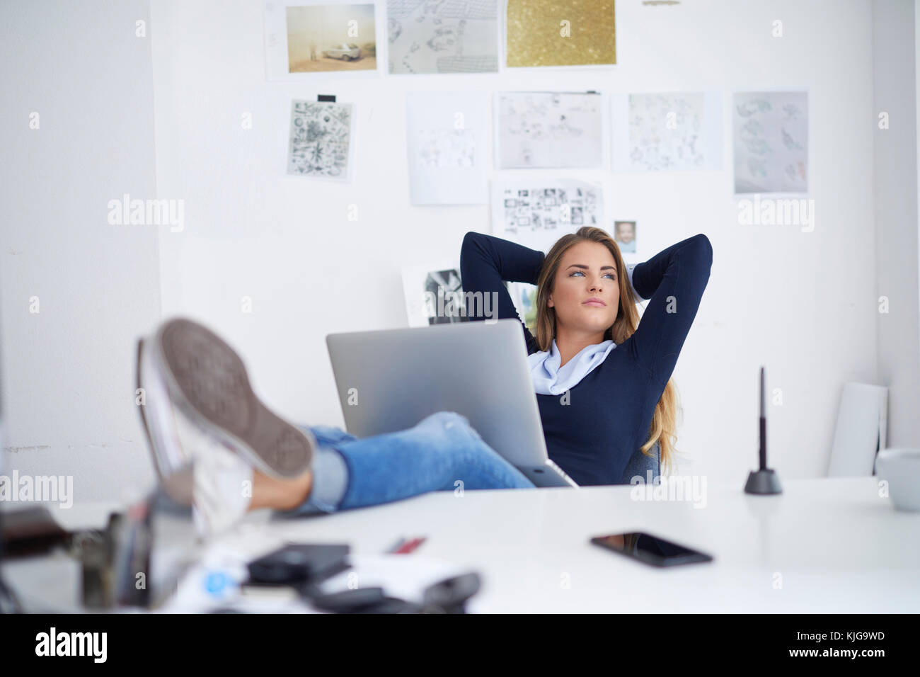 Young woman with laptop at desk in office leaning back Stock Photo - Alamy