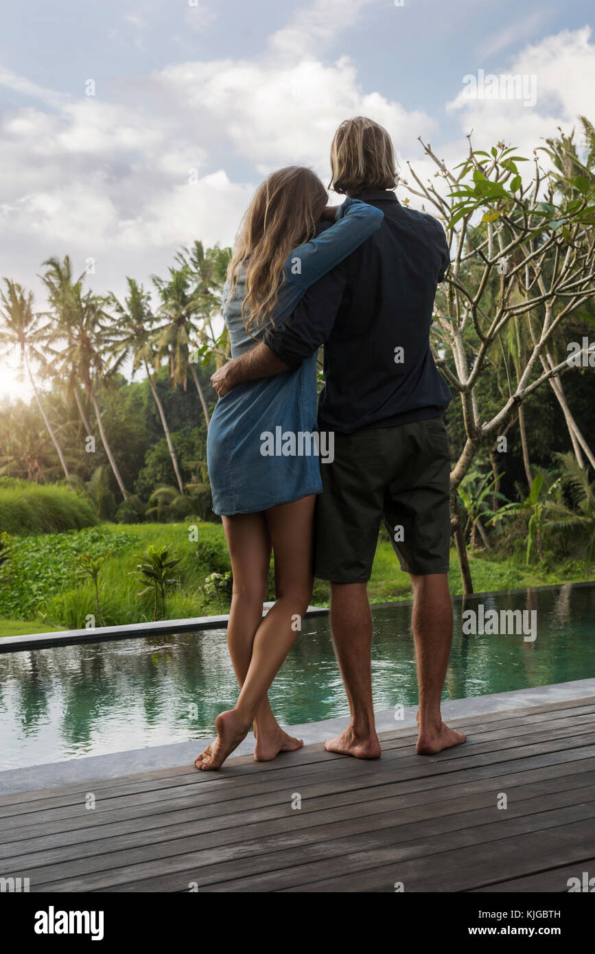 Hugging couple standing on wooden terrace in front of pool and enjoying ...