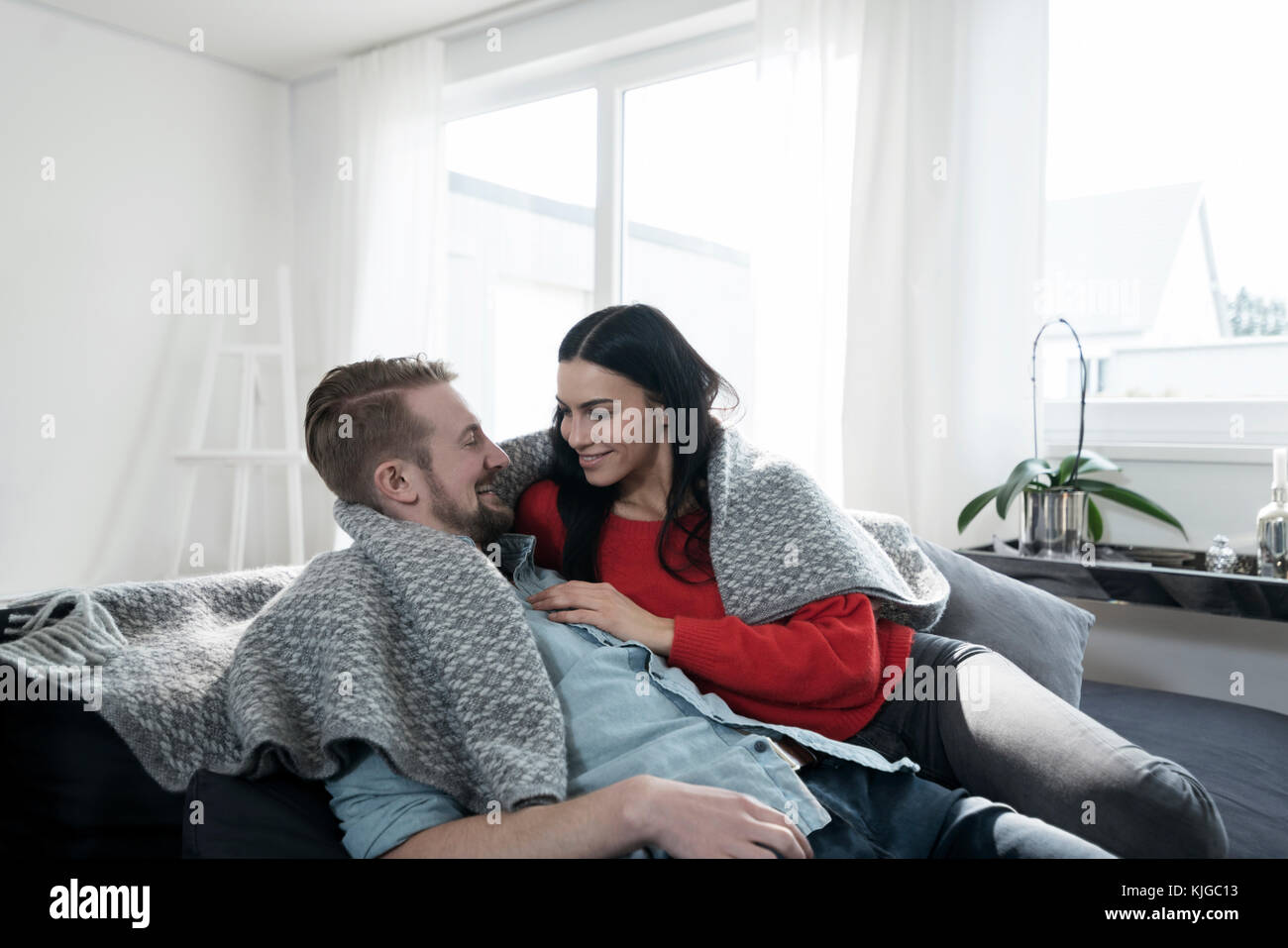 Couple cuddling under blanket on sofa in living room Stock Photo - Alamy