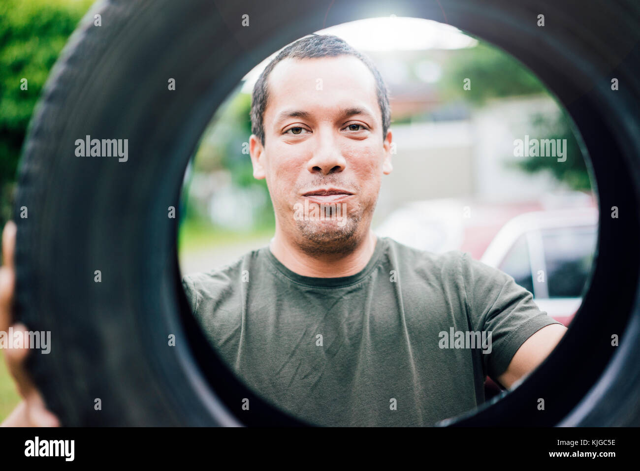 Portrait of smiling man holding car tyre Stock Photo - Alamy
