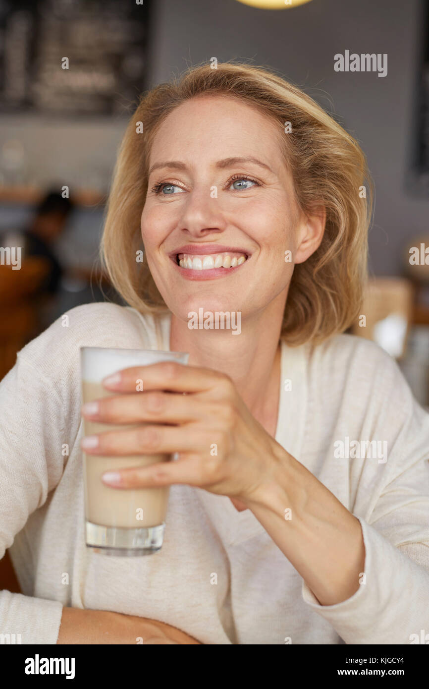 Portrait of smiling woman drinking Latte Macchiato in a coffee shop ...