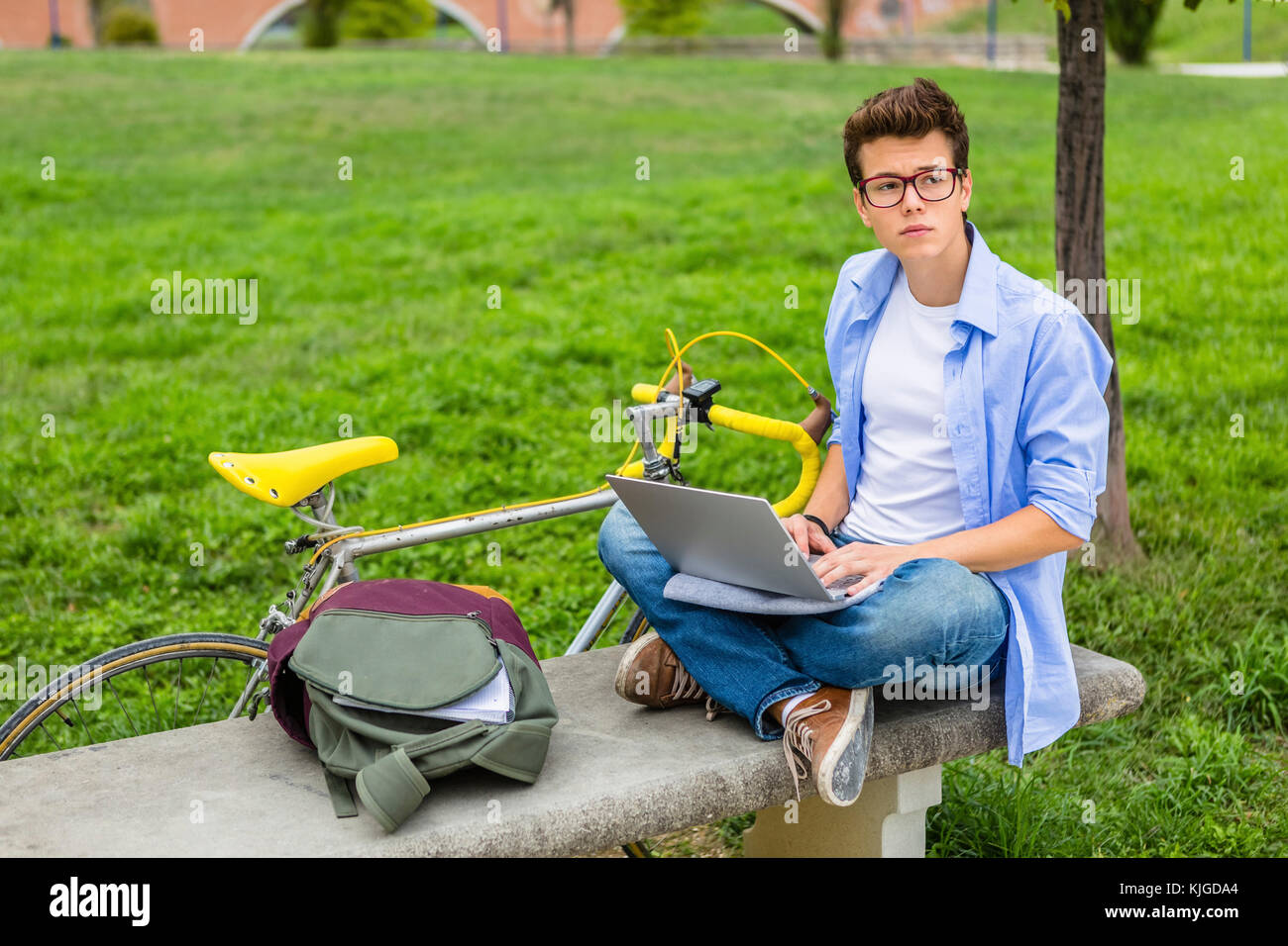 Pensive young man with racing cycle sitting on a bench using laptop ...