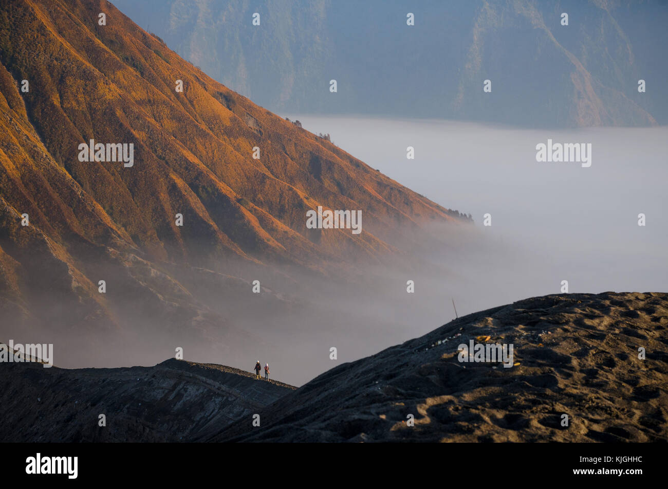 Two persons seen from behind walk along the edge of a volcano crater in ...