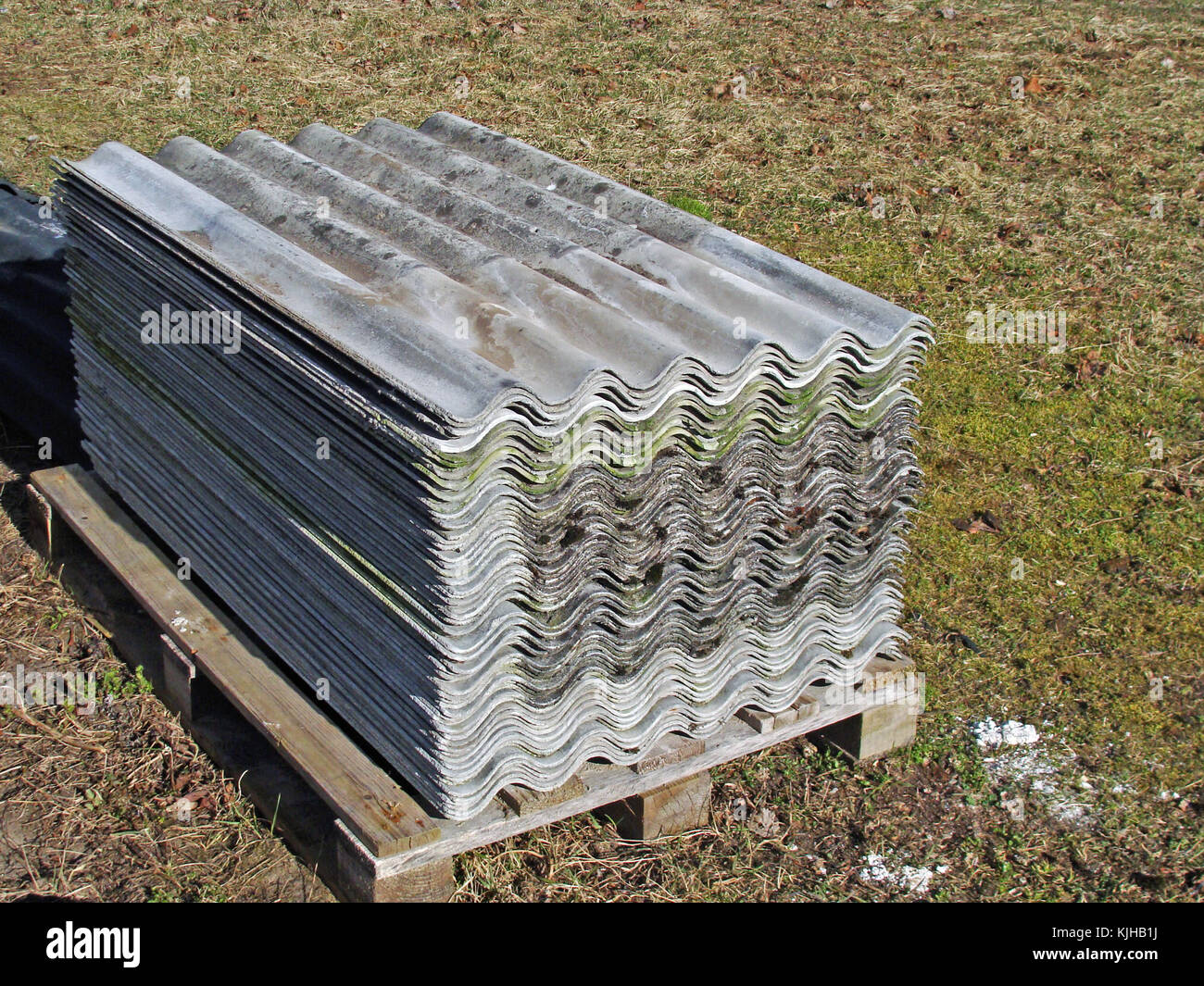 Stack of old used wavy asbestos roof tiles sheets otdoor on wooden pad ...