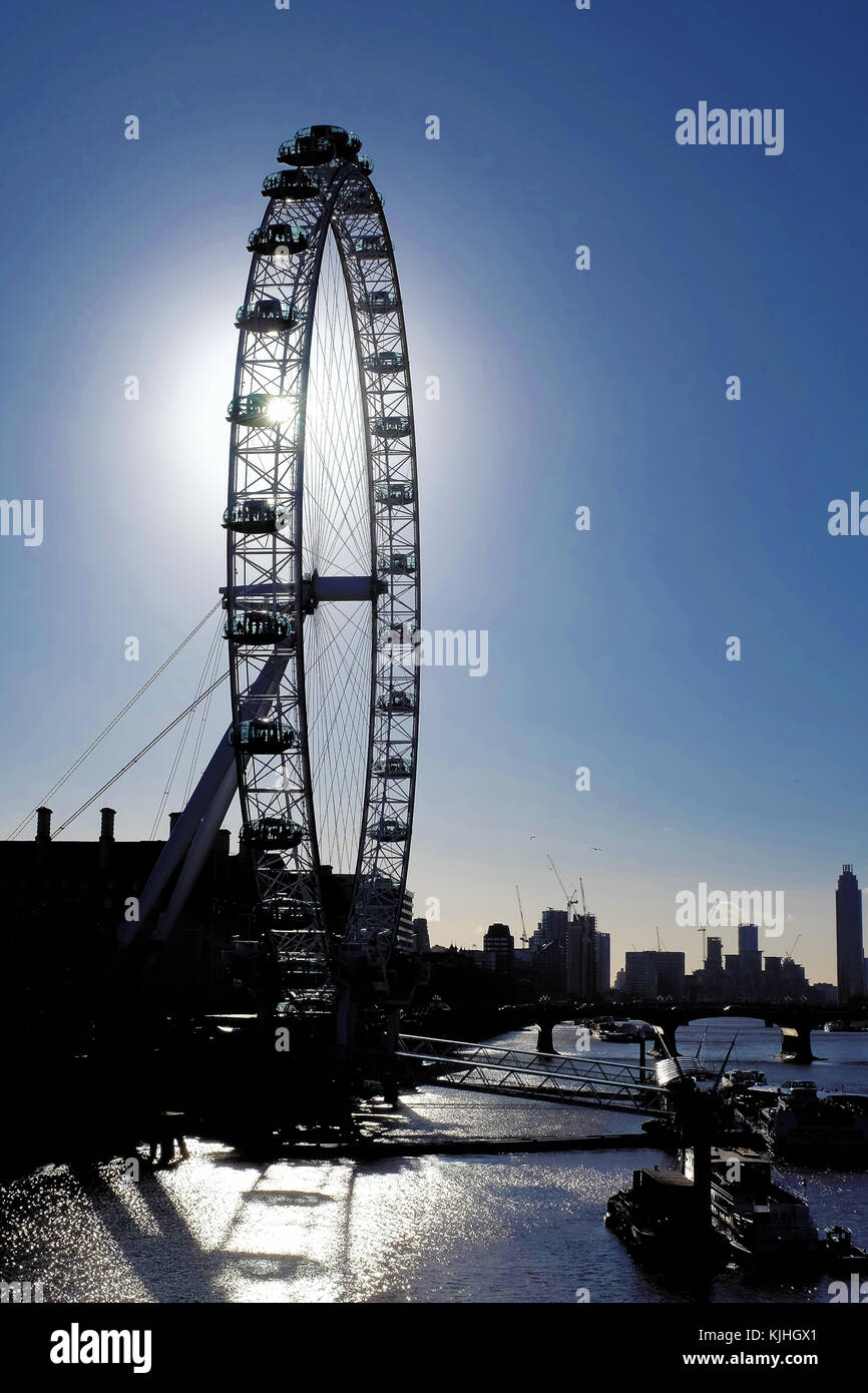 The sun shines through the London eye and reflects on the water of the ...