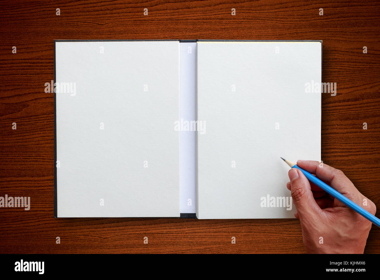Human hand use blue pencil to write open notebook put on brown wooden ...