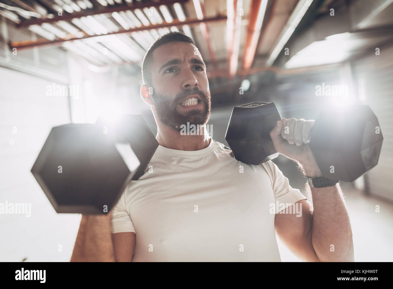 Young muscular man doing hard exercise with dumbbells for shoulders on ...
