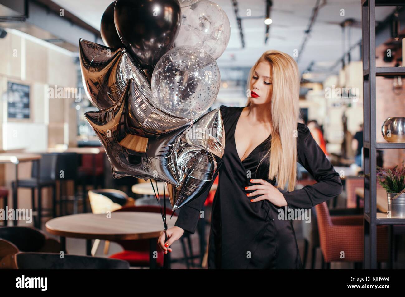 Young woman standing in a cafe holding balloons Stock Photo - Alamy