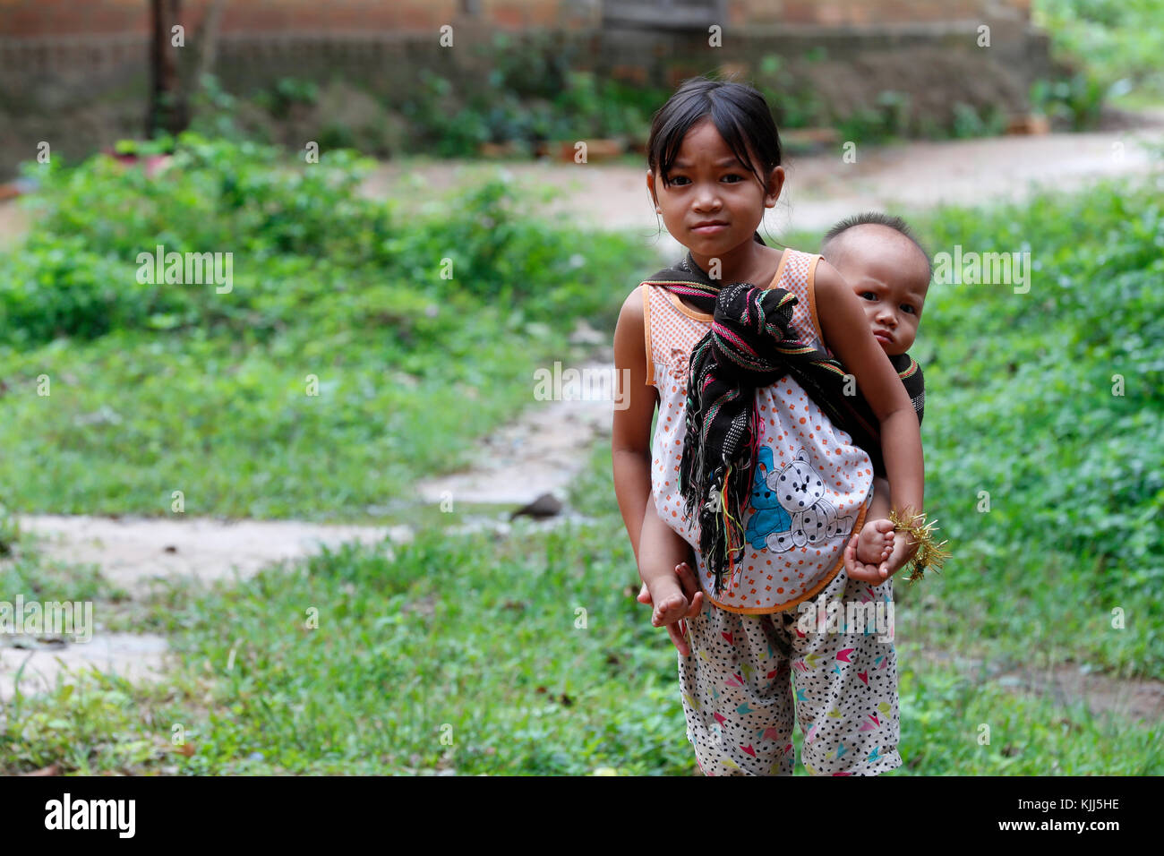 Bahnar (Ba Na) ethnic group. Young girl carrying baby on her back. Kon ...