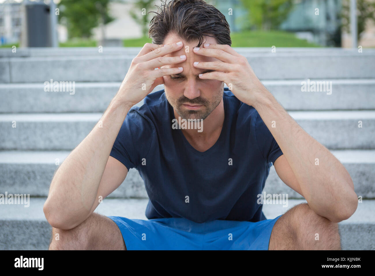 Athlete sitting on stairs with hands on head, having a headache Stock ...