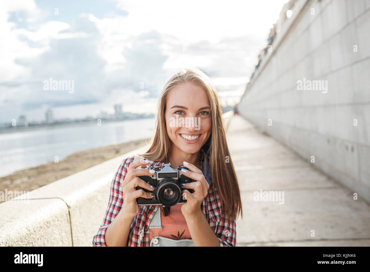 Smiling young woman with a camera at the riverside Stock Photo - Alamy