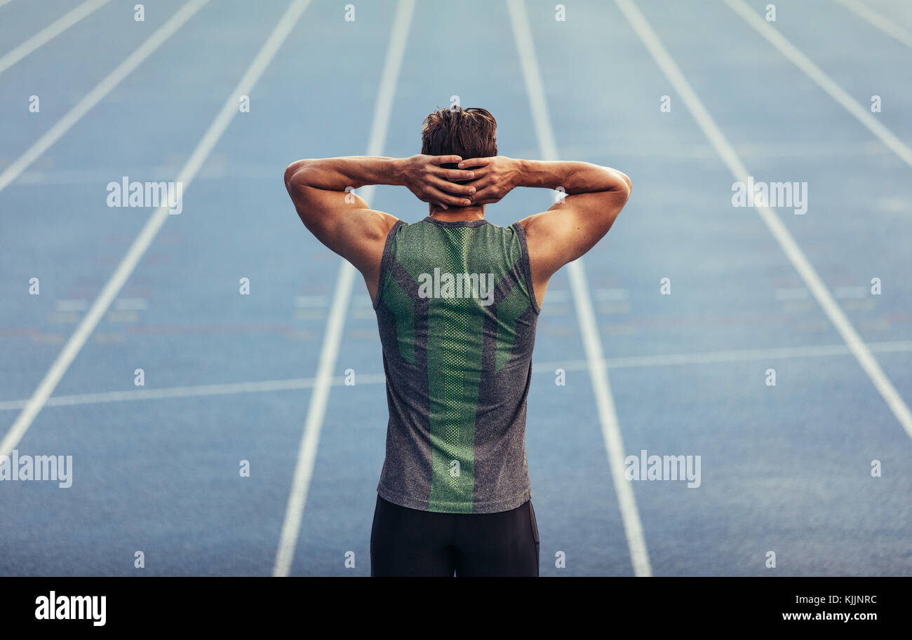 Rear view of an athlete standing on a running track with hands at the ...