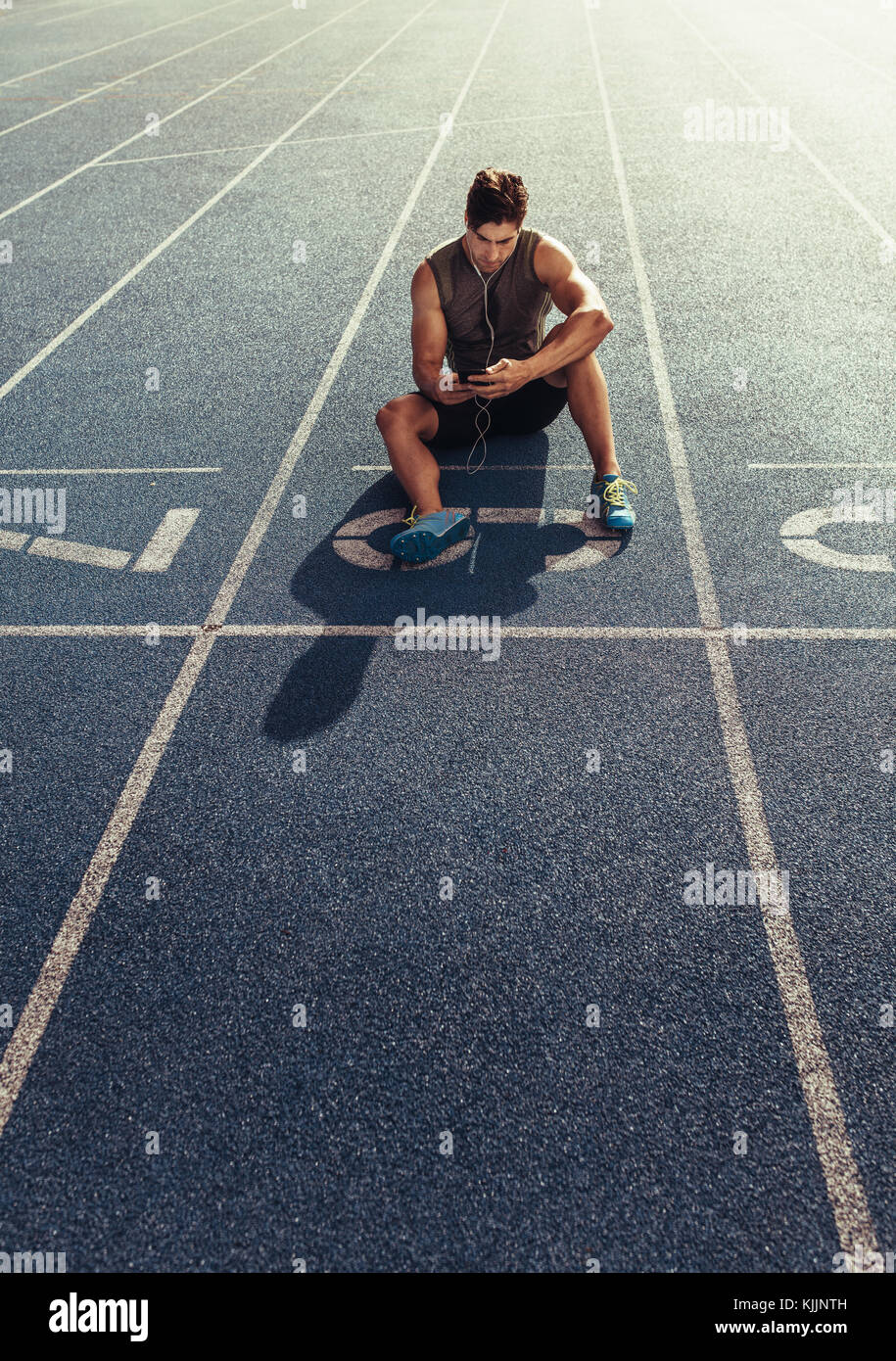 Athlete sitting on a running track listening to music. Runner wearing ...