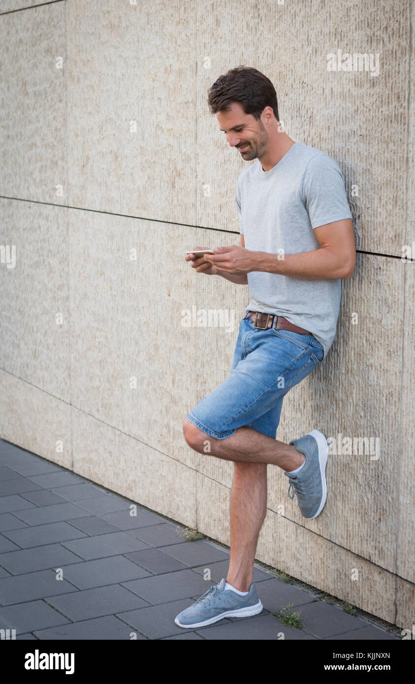 Man leaning against wall, using smartphone Stock Photo - Alamy
