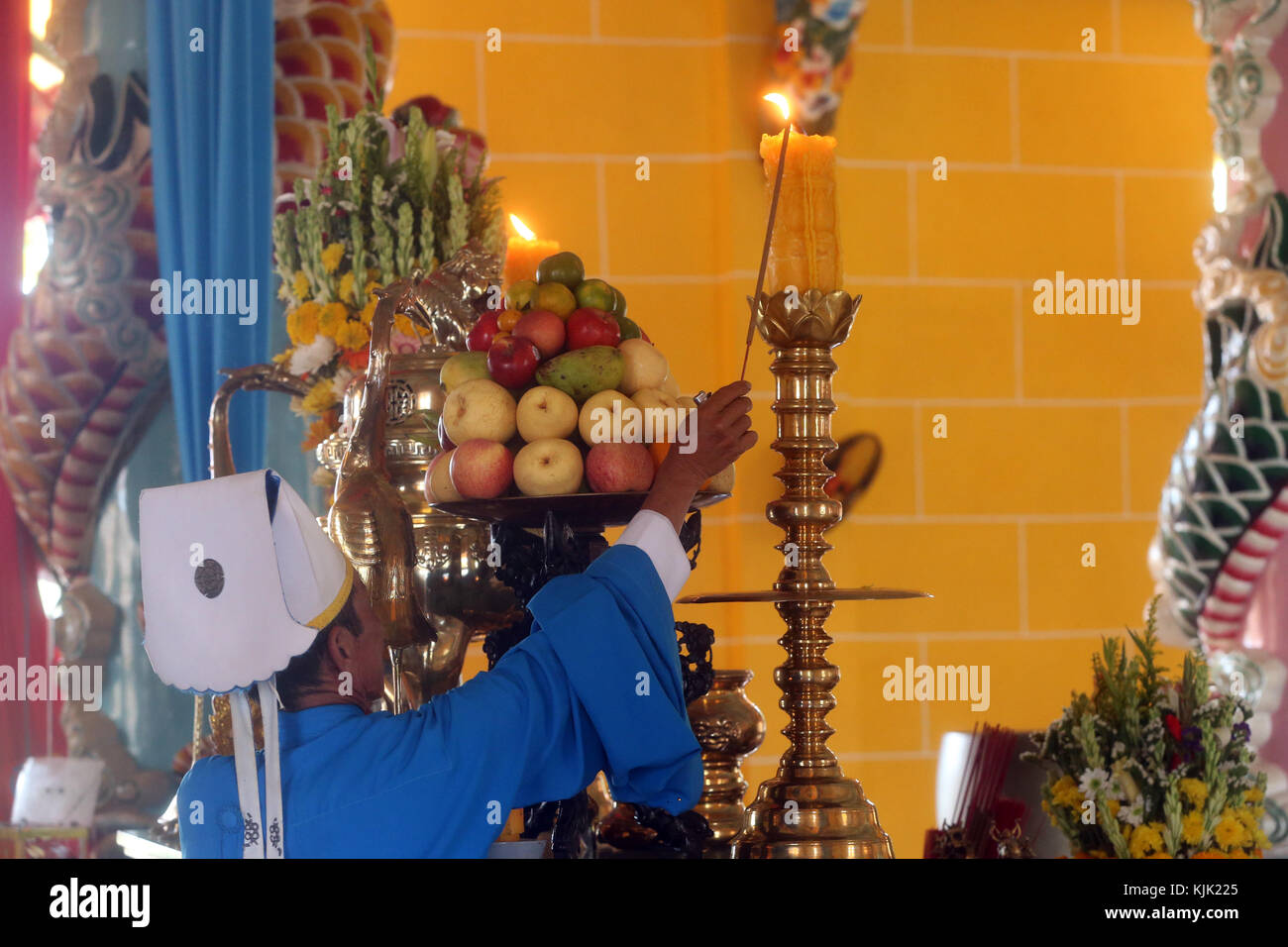 Cao Dai Holy See Temple. High priest lighting candle on altar for 12 o ...