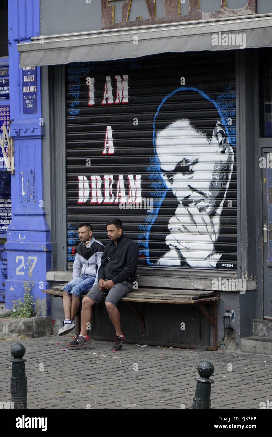 Two men sitting on a bench in front of a street artwork showing a ...