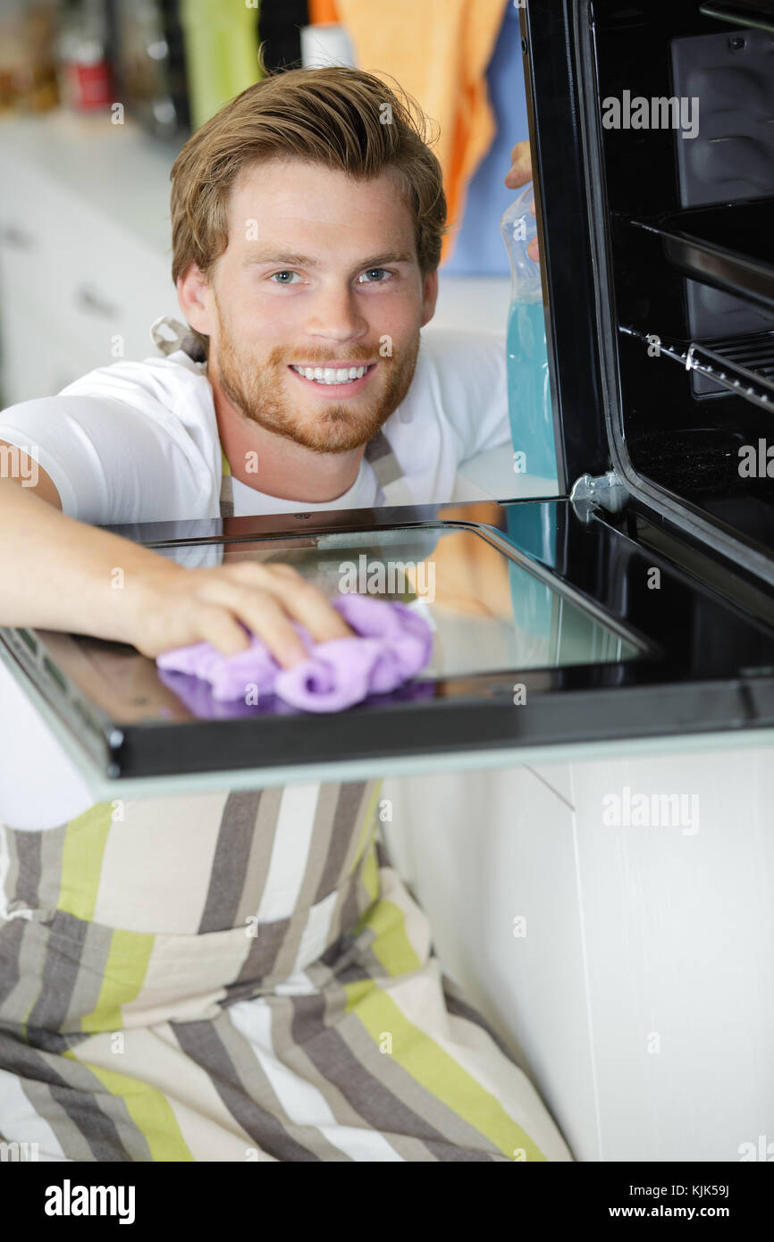 happy young man in overall cleaning oven with rag Stock Photo - Alamy