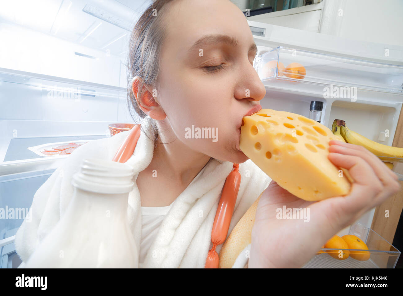 hungry young woman eating cheese near refrigerator Stock Photo - Alamy