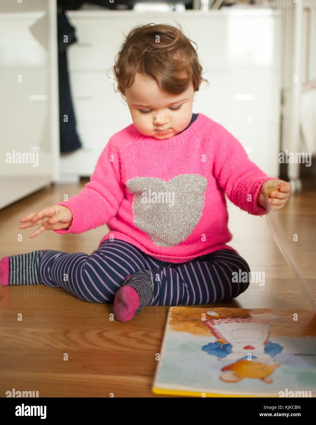 Toddler baby girl playing with fairy tales book on the oak wood floor ...