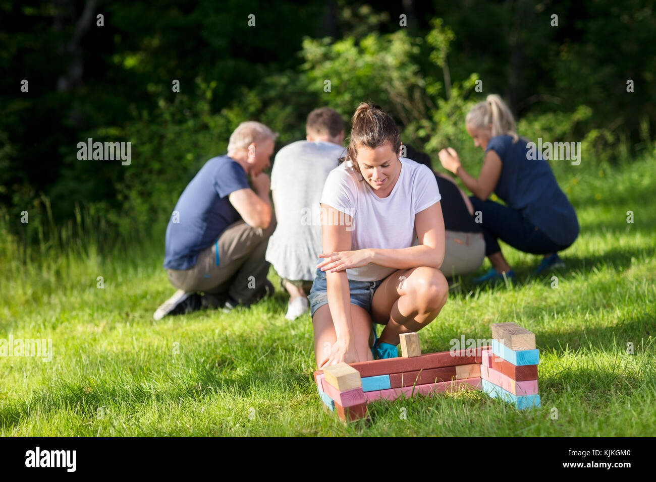 Young female crouching by building blocks while team members work in ...