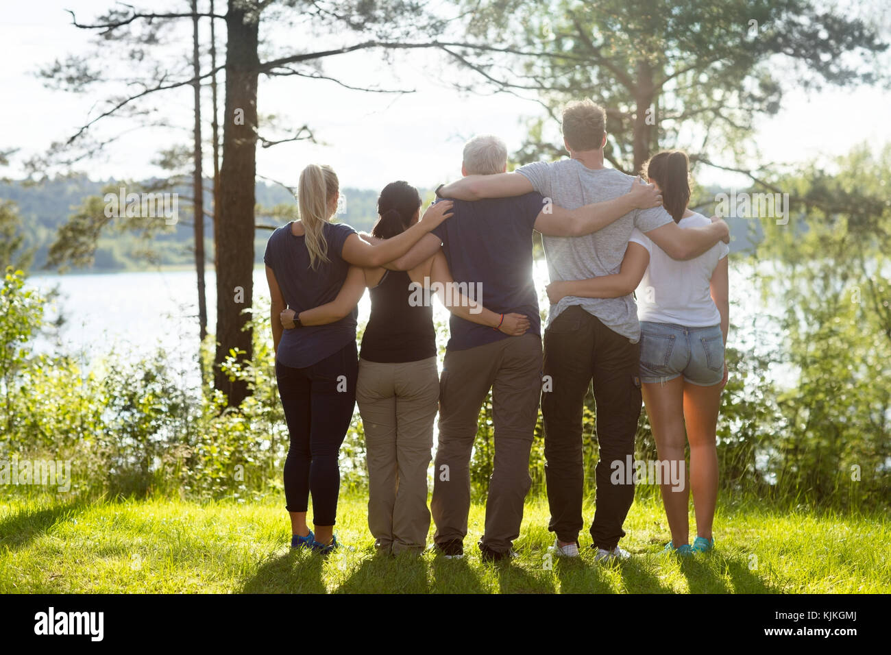 Full length rear view of male and female coworkers standing arms around ...