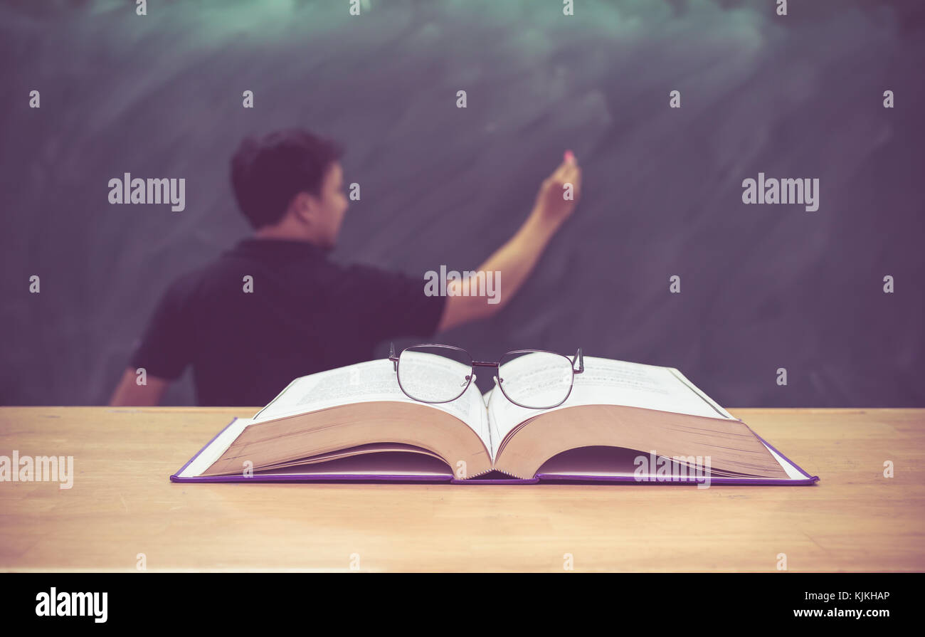 The glasses over the Books on the desk in class room with black board ...