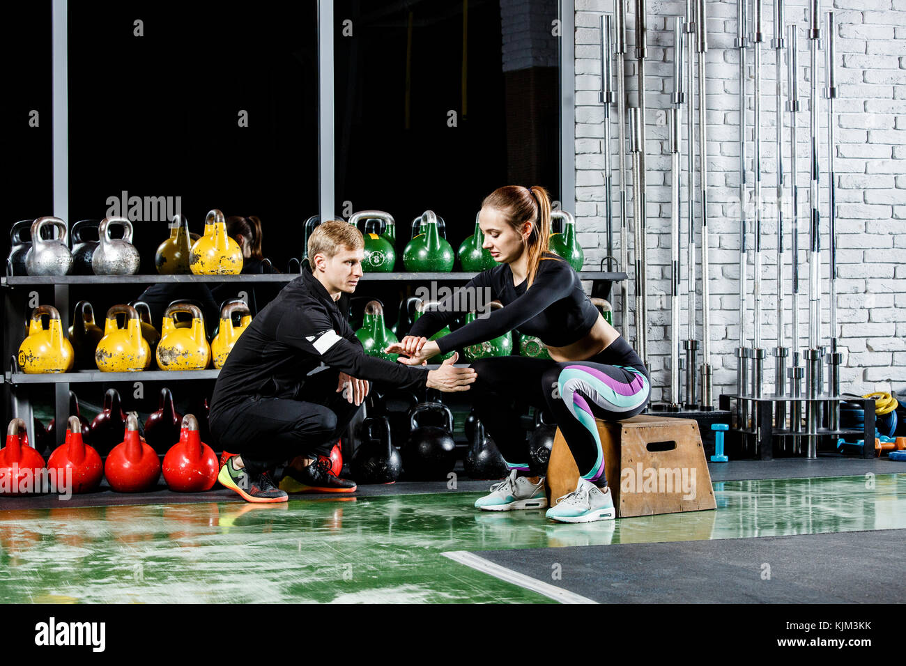 the young girl does the squat exercise in the gym with coach Stock ...