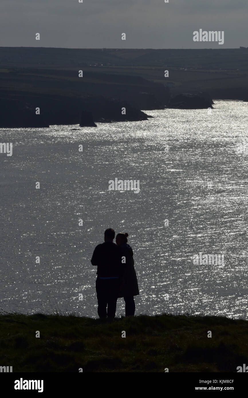 couple cuddling on the clifftops next to the sea on the Cornish coast ...