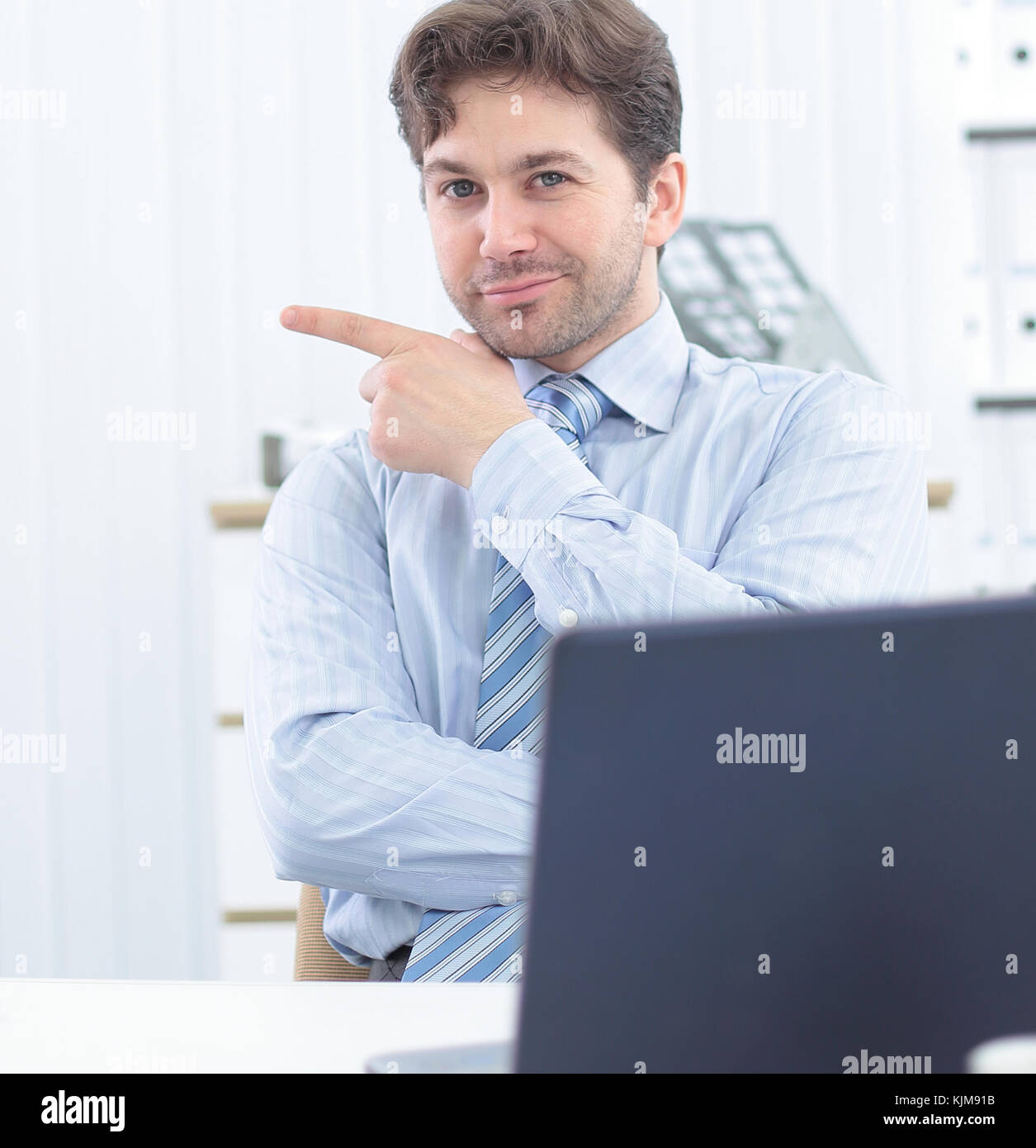 handsome businessman sitting behind a Desk and pointing to copy space ...