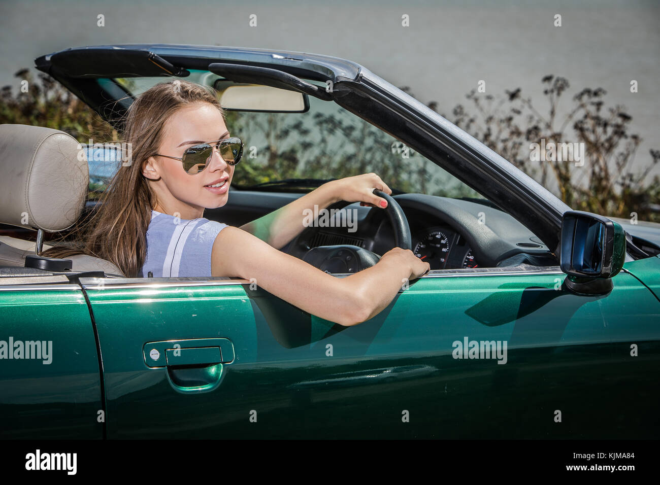 A beautiful young woman Driving her convertible car on a summer road ...